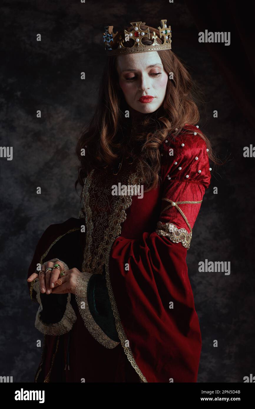 medieval queen in red dress with white makeup and crown on dark gray ...