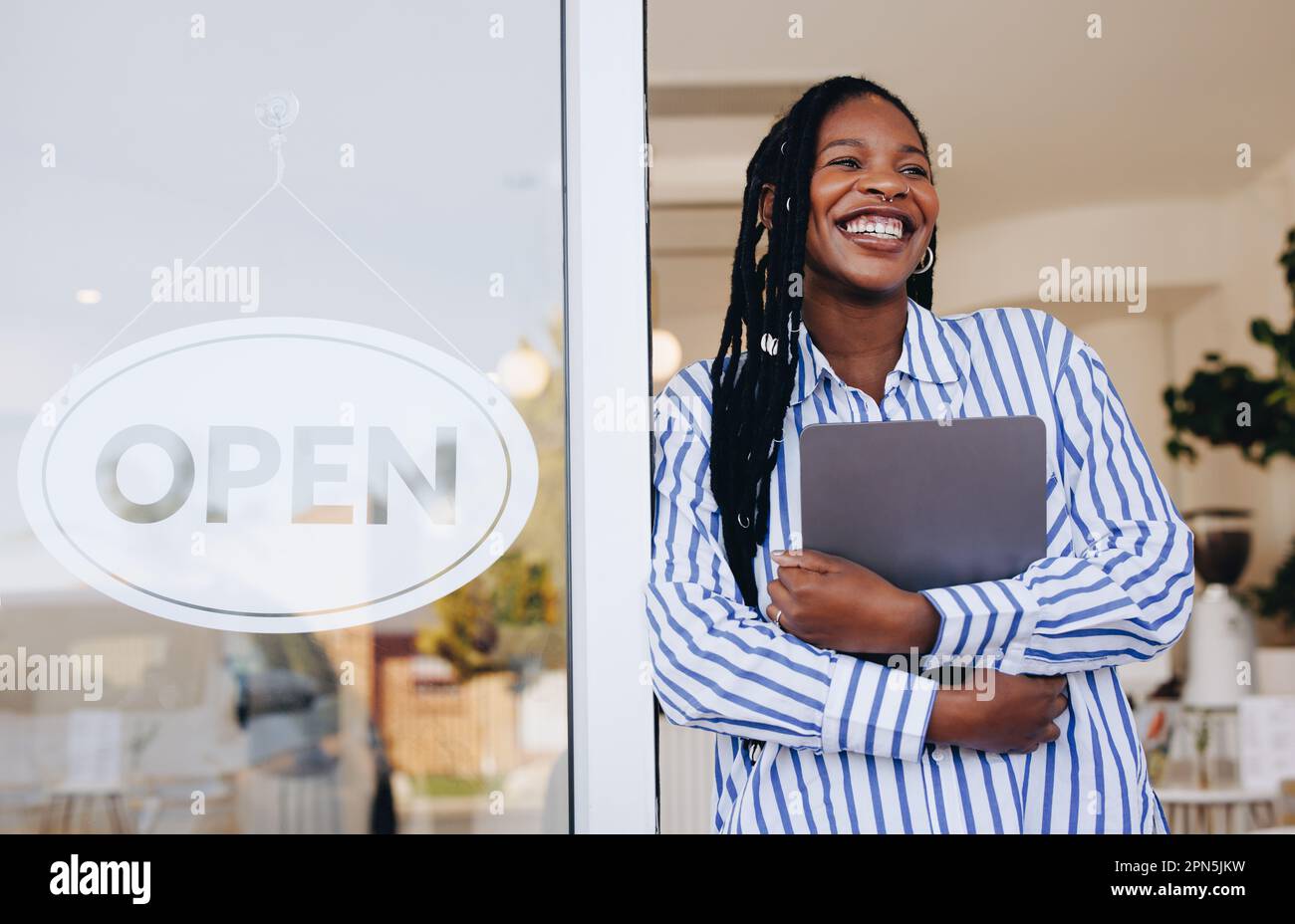Successful young cafe owner standing next to an open sign at the ...