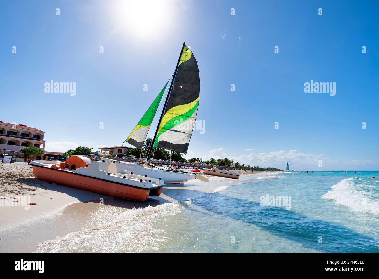A sailing catamaran is parked on the white sand on the seashore against ...