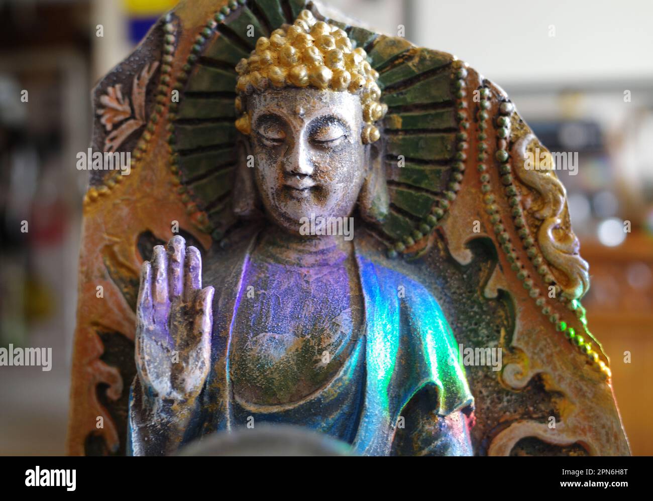 Small Buddha statue in refracting light. He lifts his hand in the ...