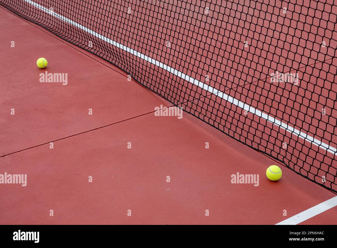 two balls next to the net of a red tennis court Stock Photo - Alamy