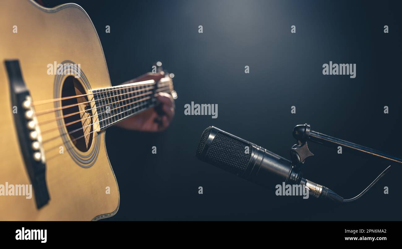 Male musician playing acoustic guitar behind microphone in recording ...