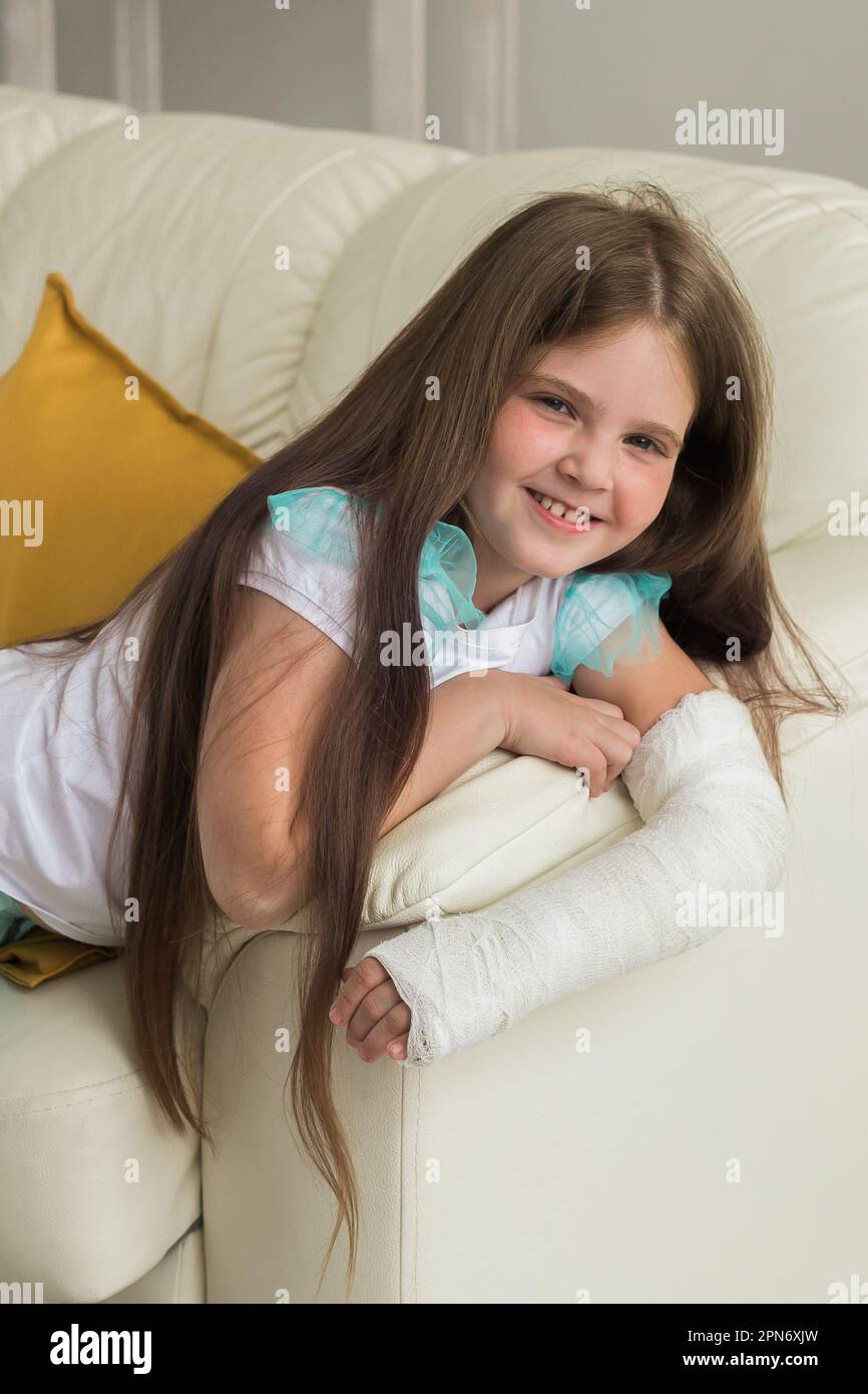 Child with a cast on a broken wrist or arm sits on a couch. Recovery ...