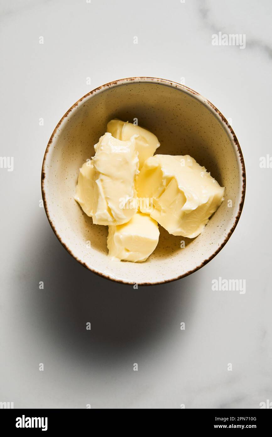 Unsalted butter cubes in white bowl on white marble background. The oil ...