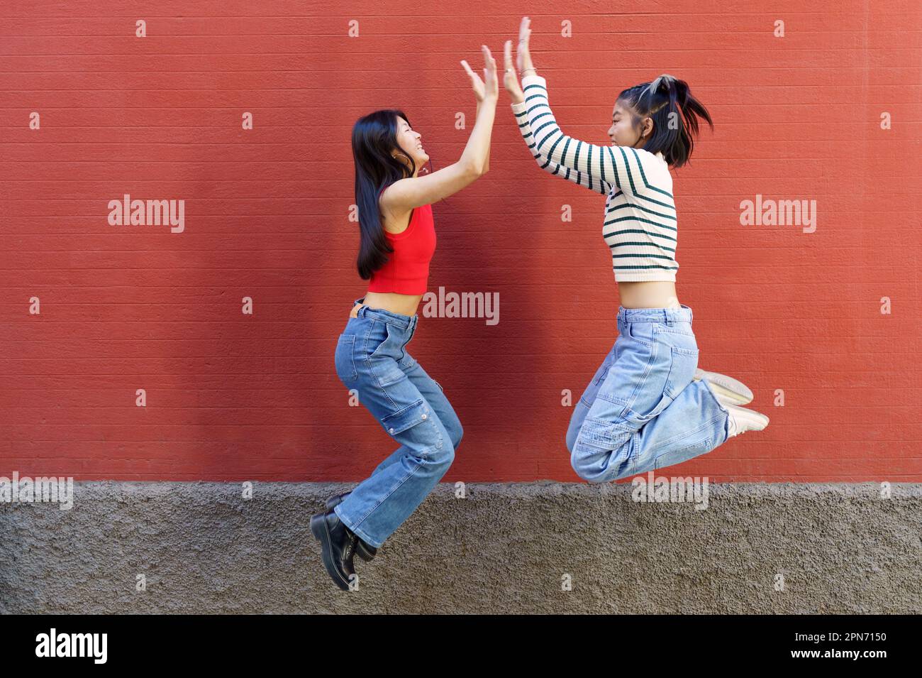 Joyful young Asian girlfriends giving high five while jumping Stock ...