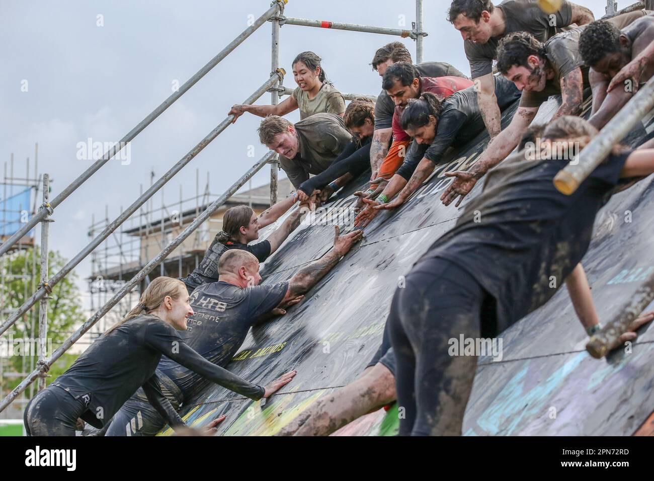 Participants try to climb up on a slippery surface during Tough Mudder ...