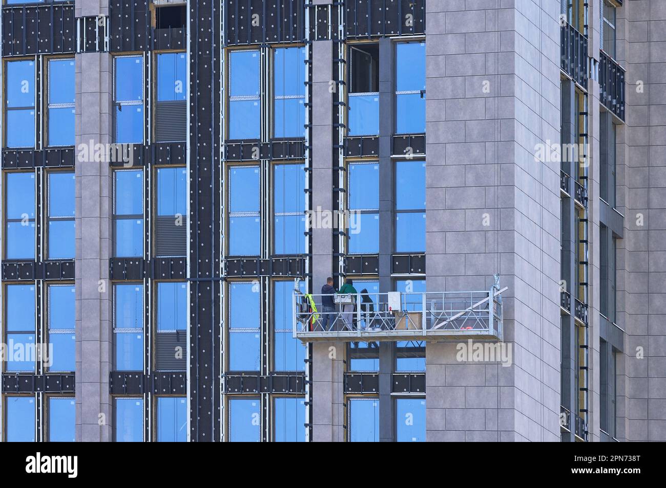 A team of workers on a suspended cradle performs edging facade work in ...
