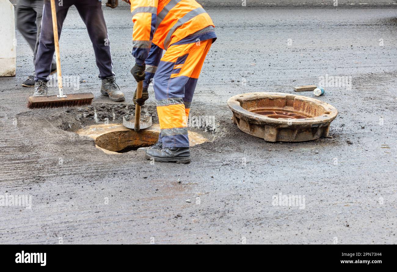 A team of road workers in orange-and-blue overalls is repairing a sewer ...
