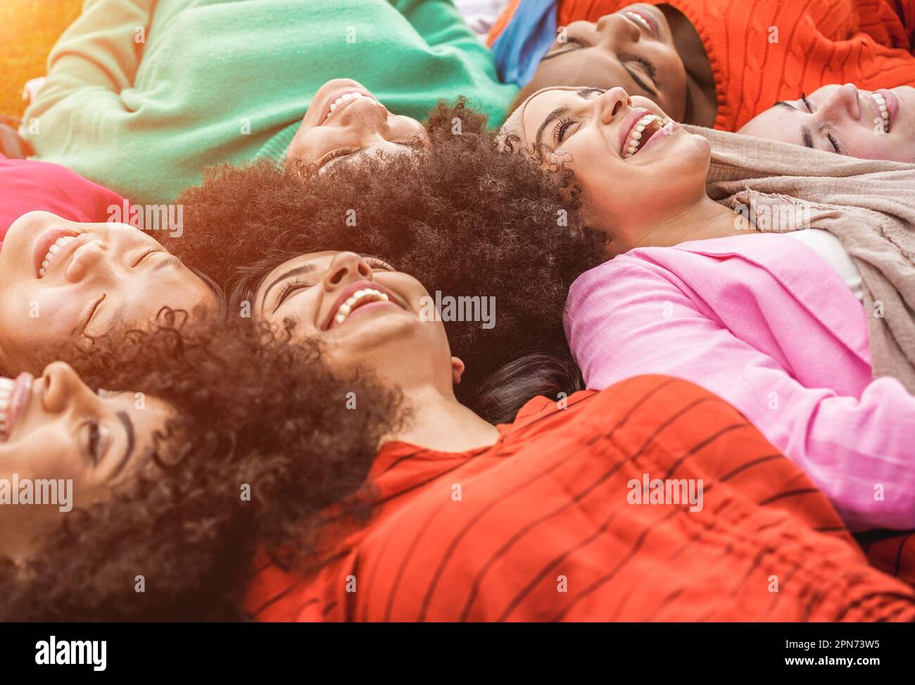 Happy diverse female friends having fun lying together in circle outdoor - Focus on arabian girl ...