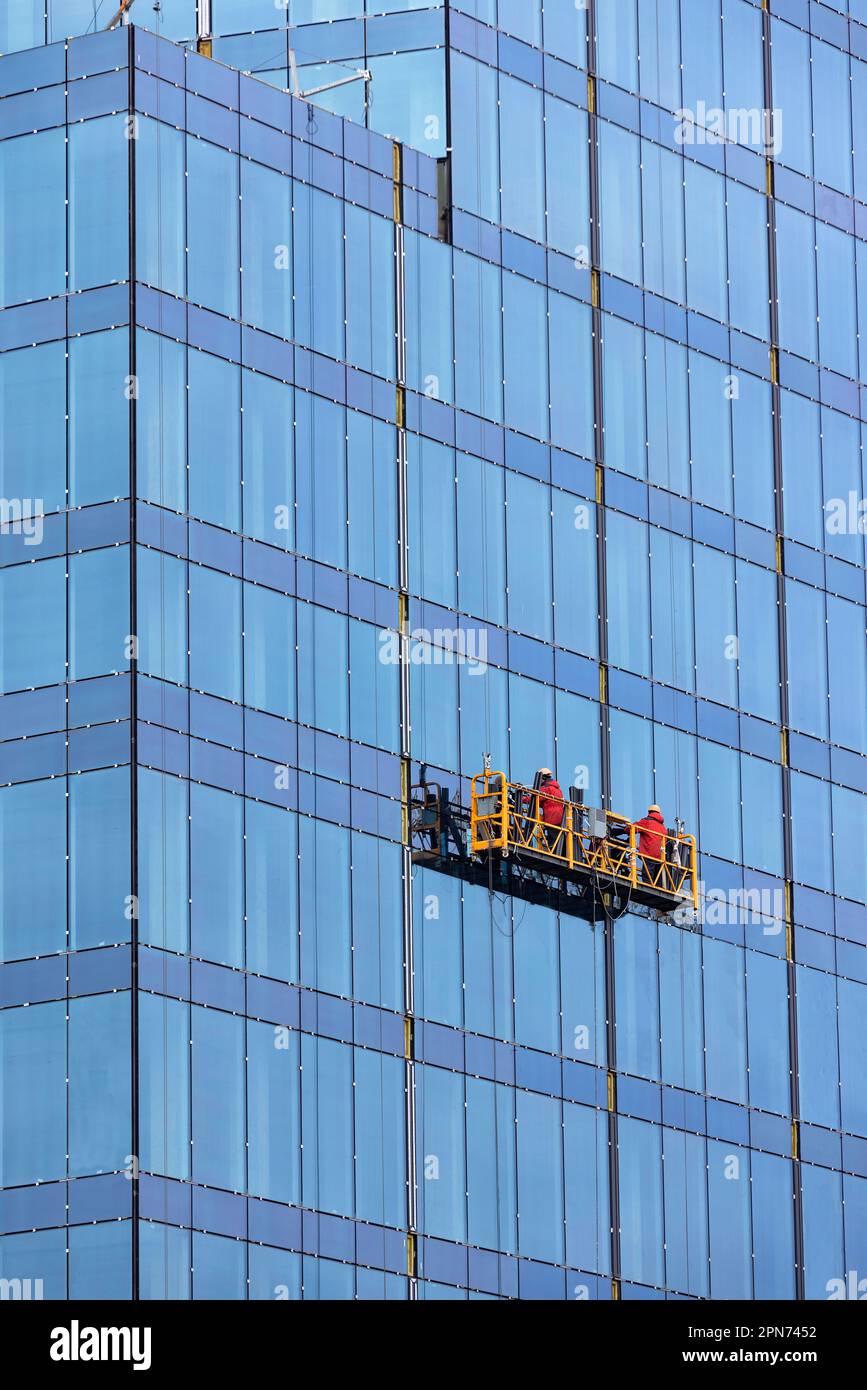 Builders in red overalls are mounting the glass facade of a multi ...