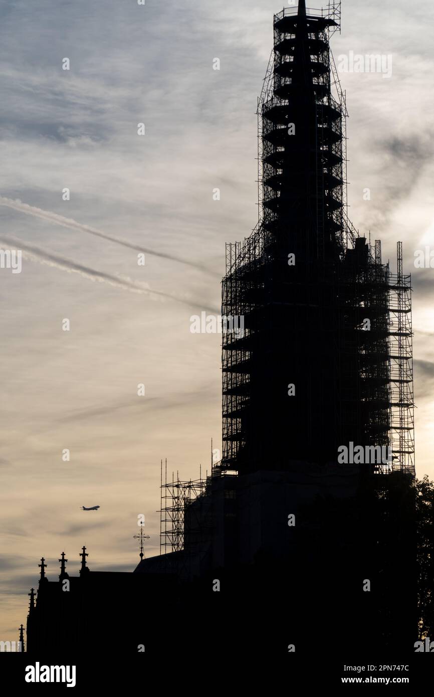 A plane flying very close to a building under construction. Sun rising ...