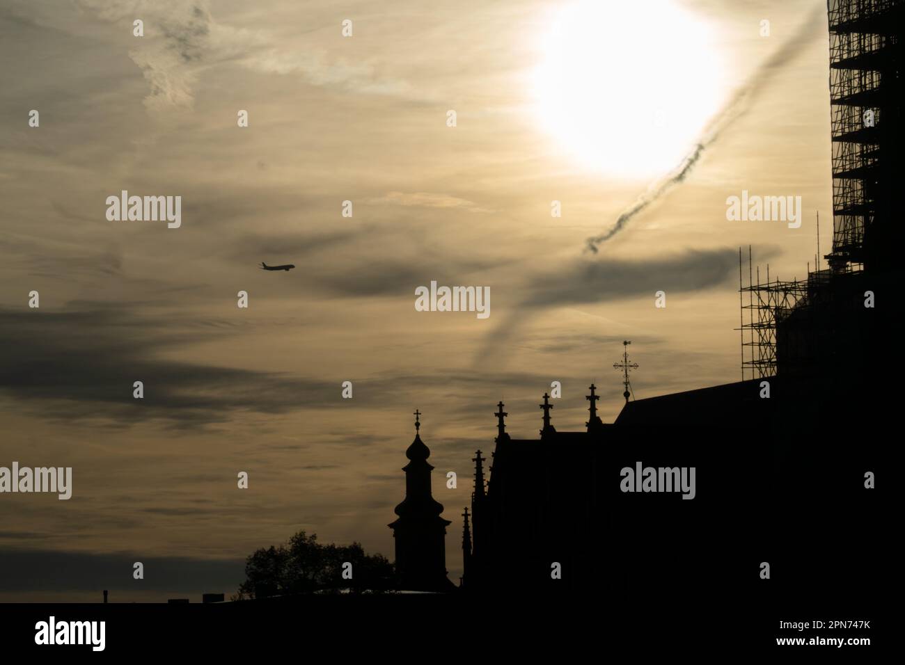 A plane flying very close to a building under construction. Sun rising ...