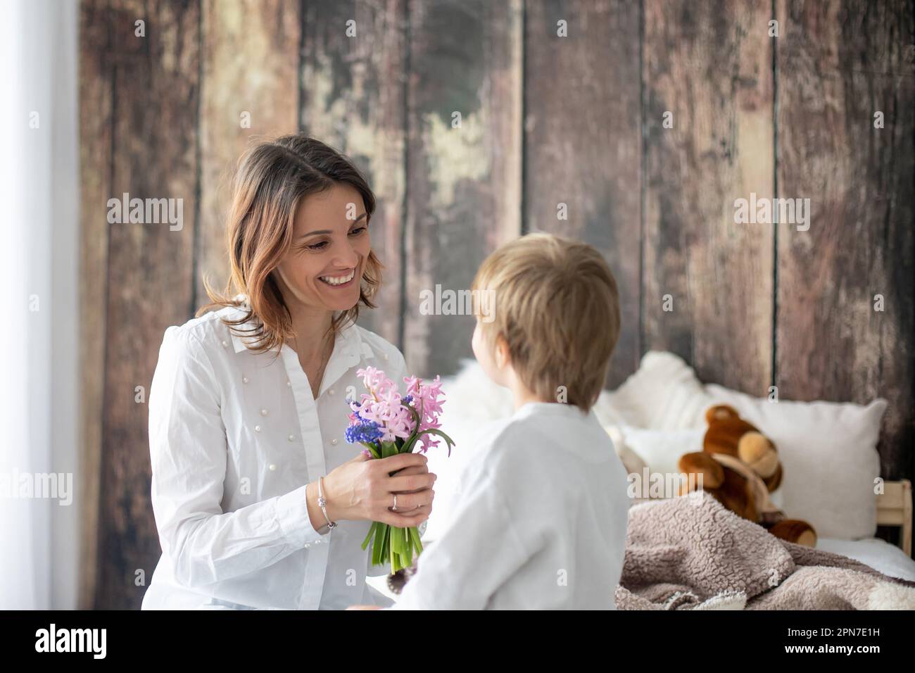 Cute little boy, giving flowers to his mom for Mothers day at home ...