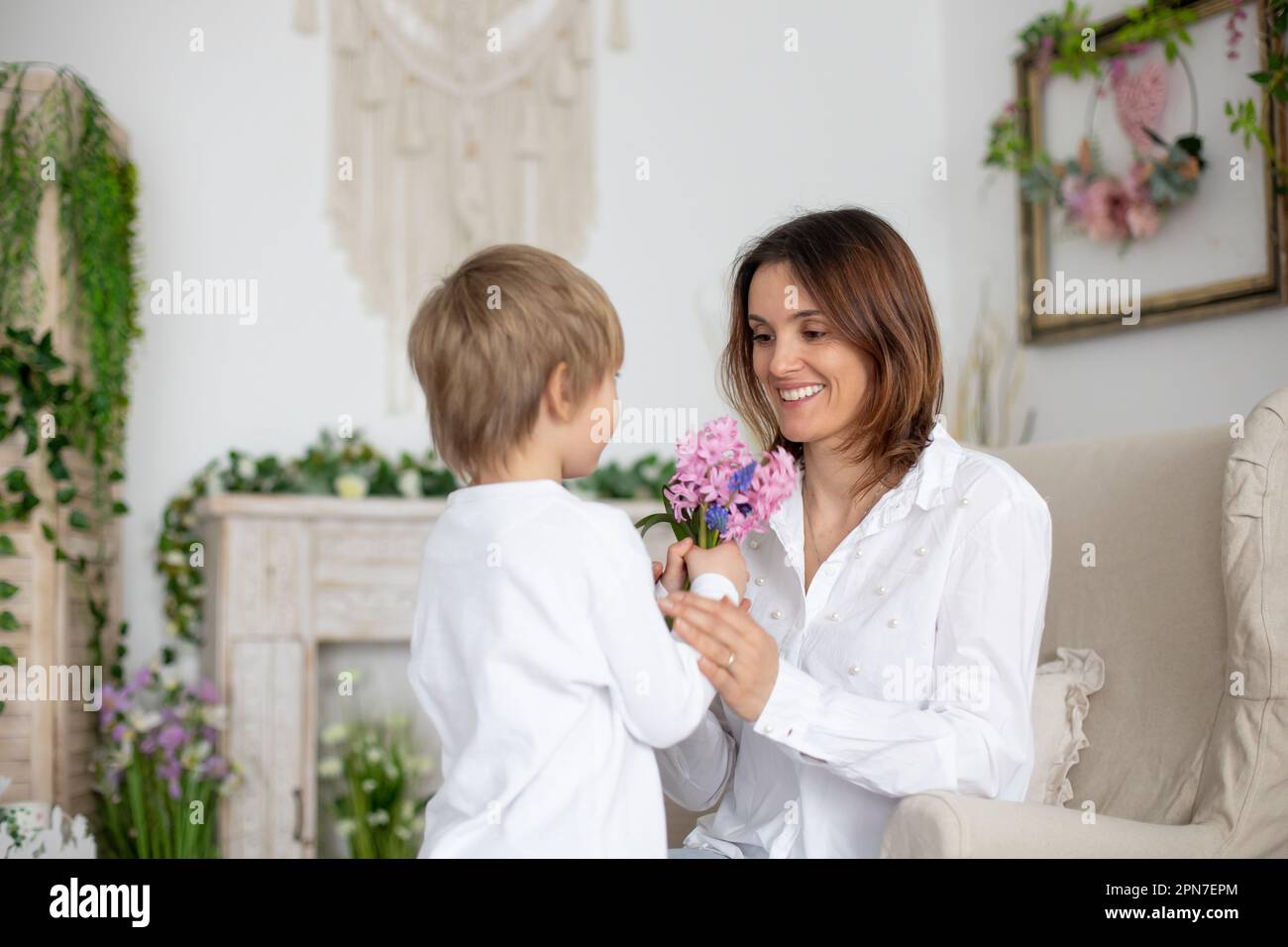 Cute little boy, giving flowers to his mom for Mothers day at home ...