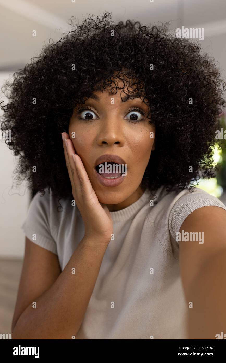 Portrait of surprised biracial woman with afro at home making video ...