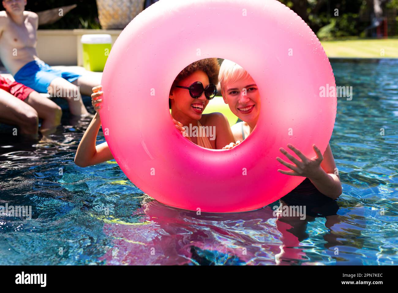 Portrait of happy diverse female friends having pool party, holding ...