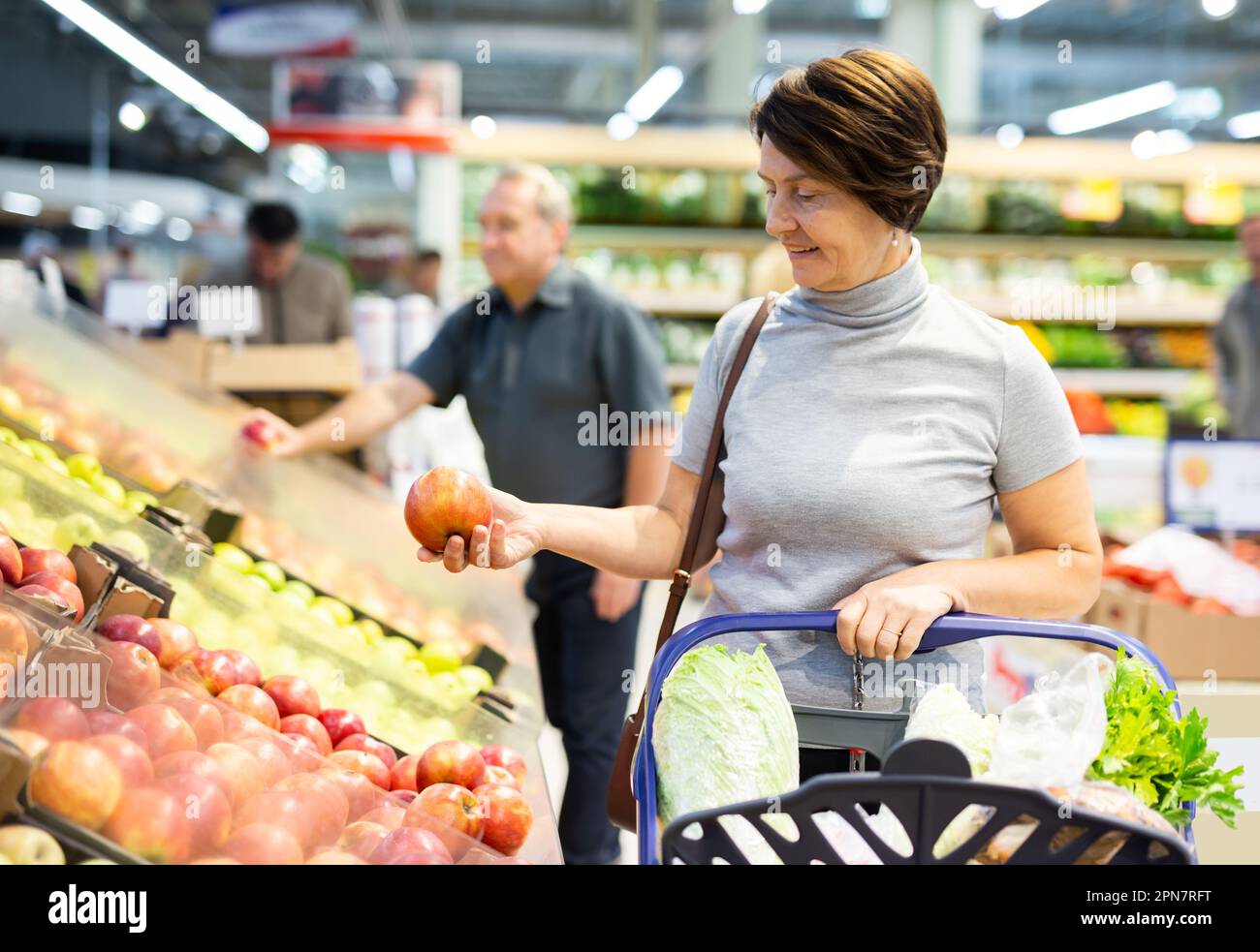 Positive woman chooses ripe red apples on grocery store window Stock ...