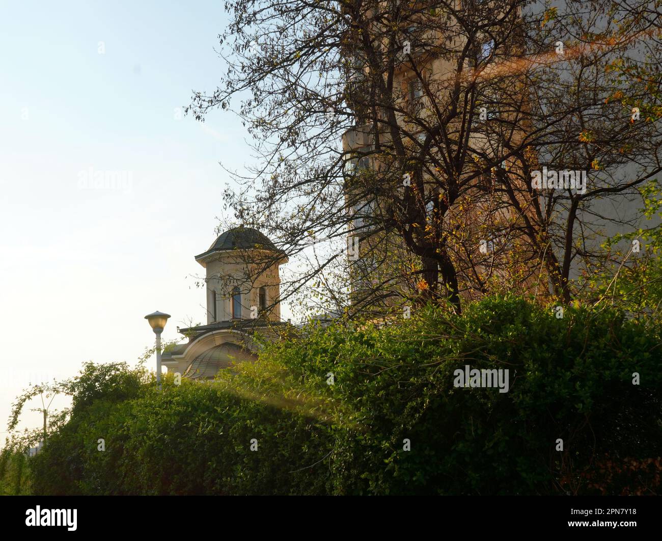 Christian ortodox church near tall block of flats beyond green hedge ...