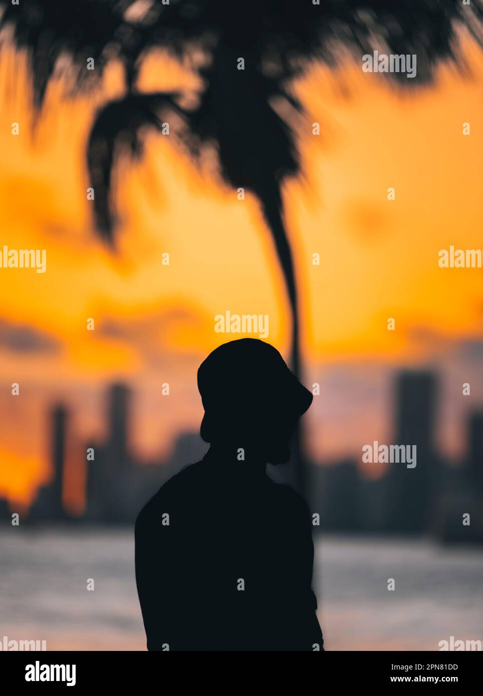 A silhouette of a male with a bucket hat against a sunset beach ...
