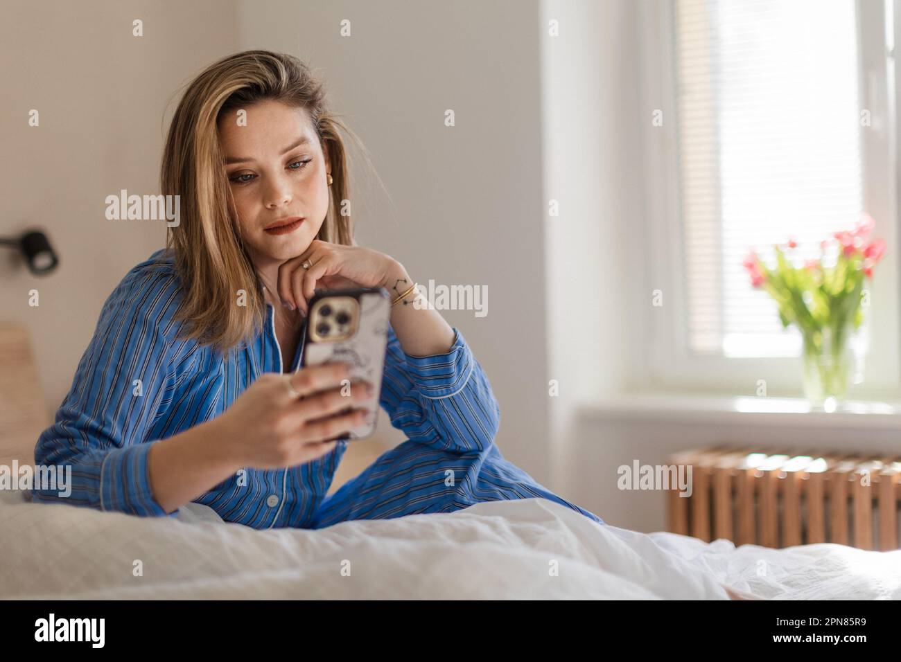 Young woman lying on a bed and scrolling her smartphone Stock Photo - Alamy