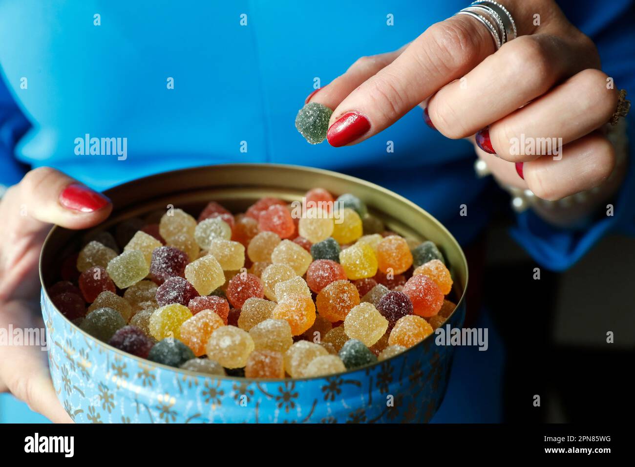 A woman hand taking a candy from a blue box full of fruit drop candies ...