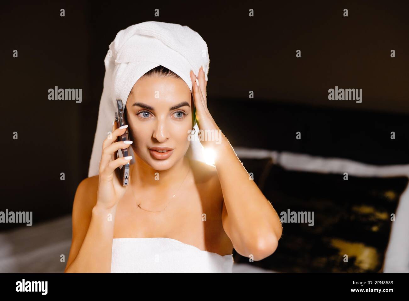 Pretty young woman wrapped in a shower towel using mobile phone while ...