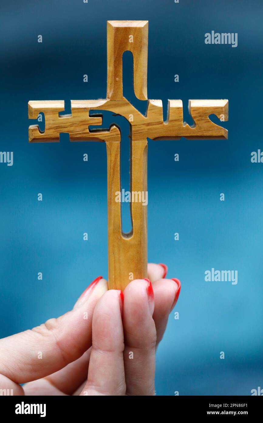 Woman praying to God, holding a wooden christian cross with the name of ...
