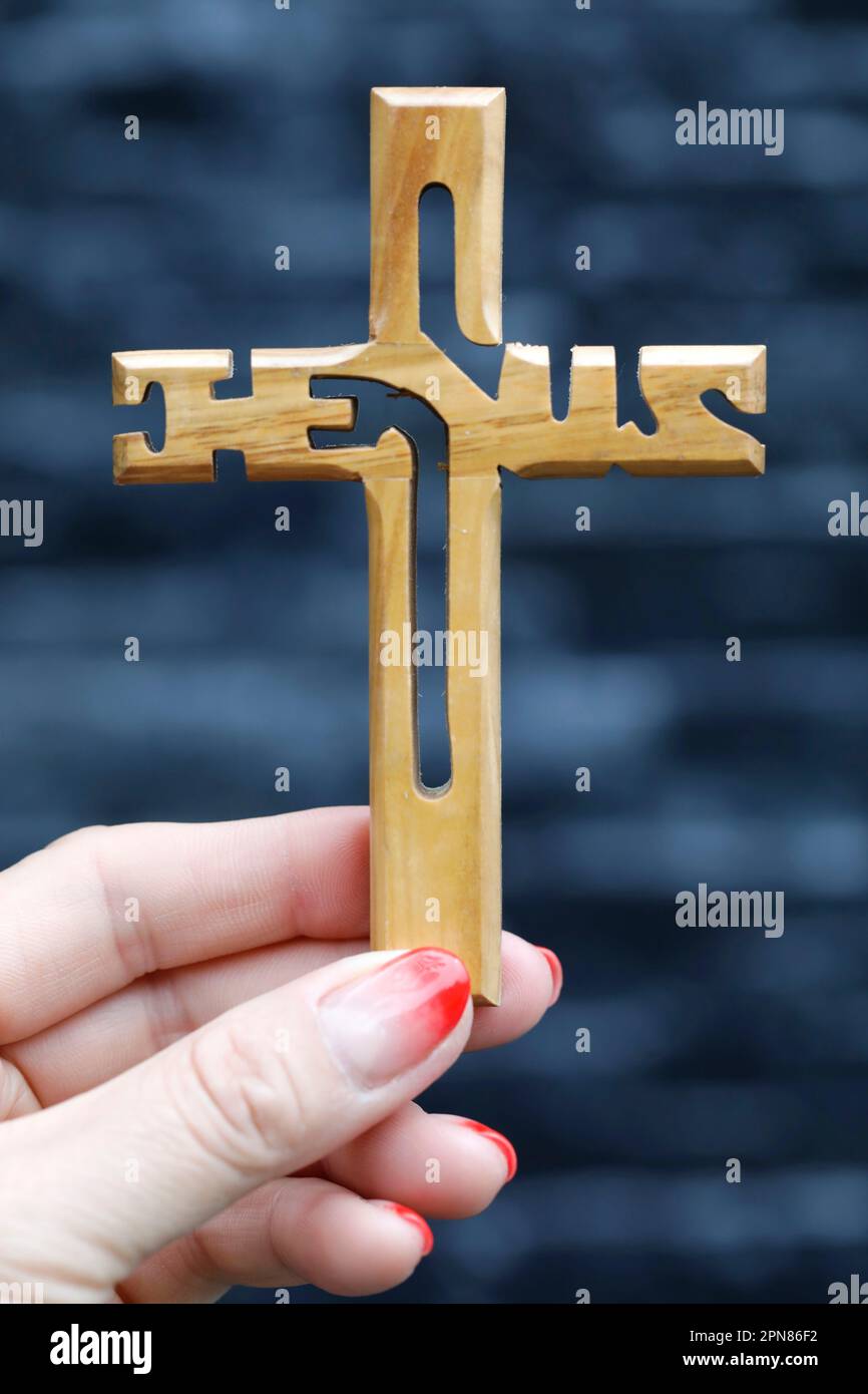 Woman praying to God, holding a wooden christian cross with the name of ...