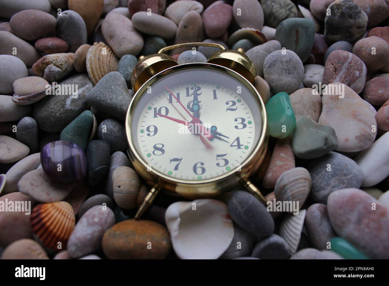 Old copper alarm clock on smooth colored pebbles and seashells Stock ...