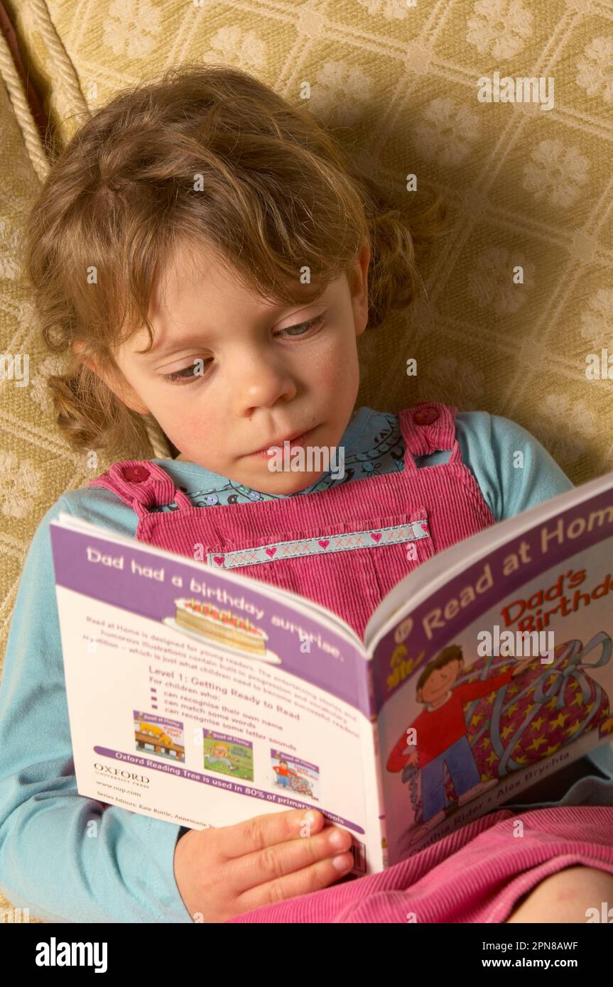 Girl reading a story book in a comfy chair Stock Photo - Alamy