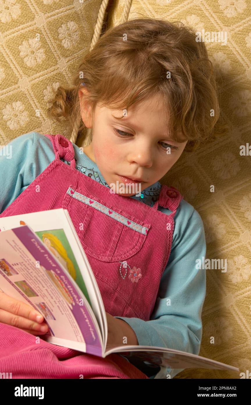 Girl reading a book in a comfy chair Stock Photo - Alamy