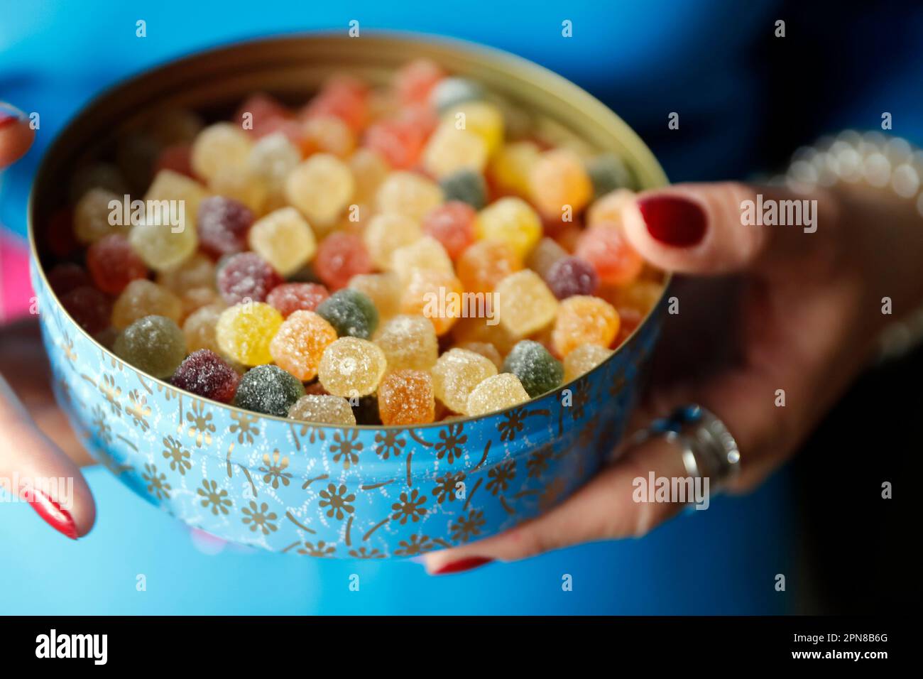 A woman hand taking a candy from a blue box full of fruit drop candies ...