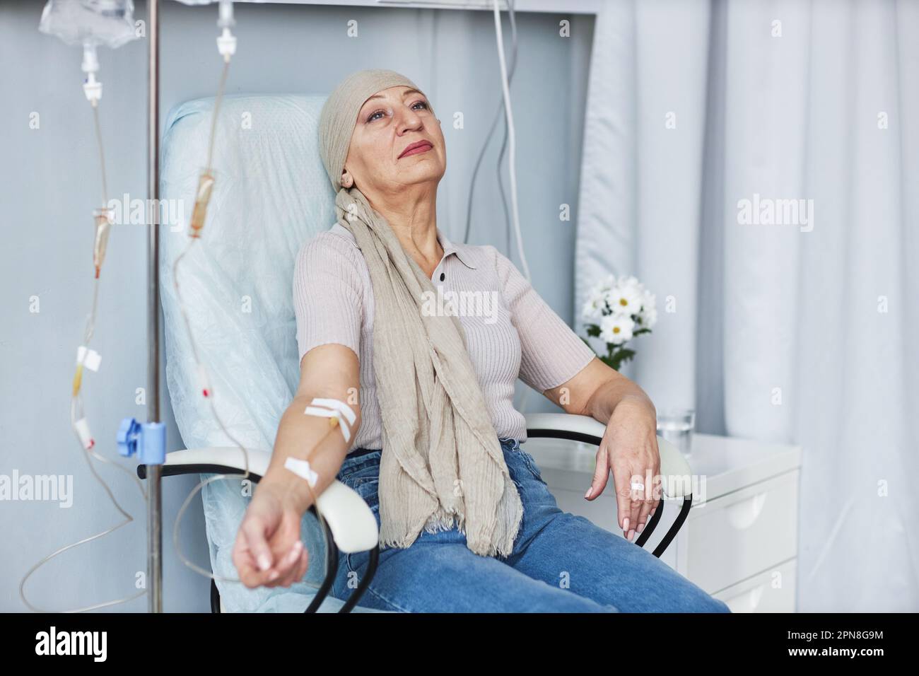 Portrait of tired senior woman sitting in chair with IV drip during ...