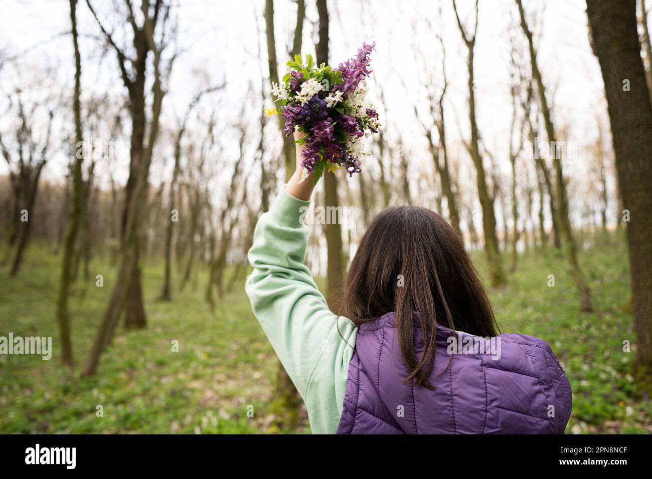 Back view of woman with hand up hold spring bouquet of flowers on ...