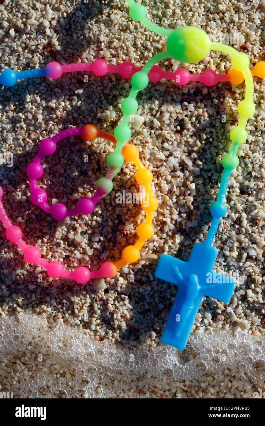 A plastic crucifix and a rosary with beads partially buried in the sand ...
