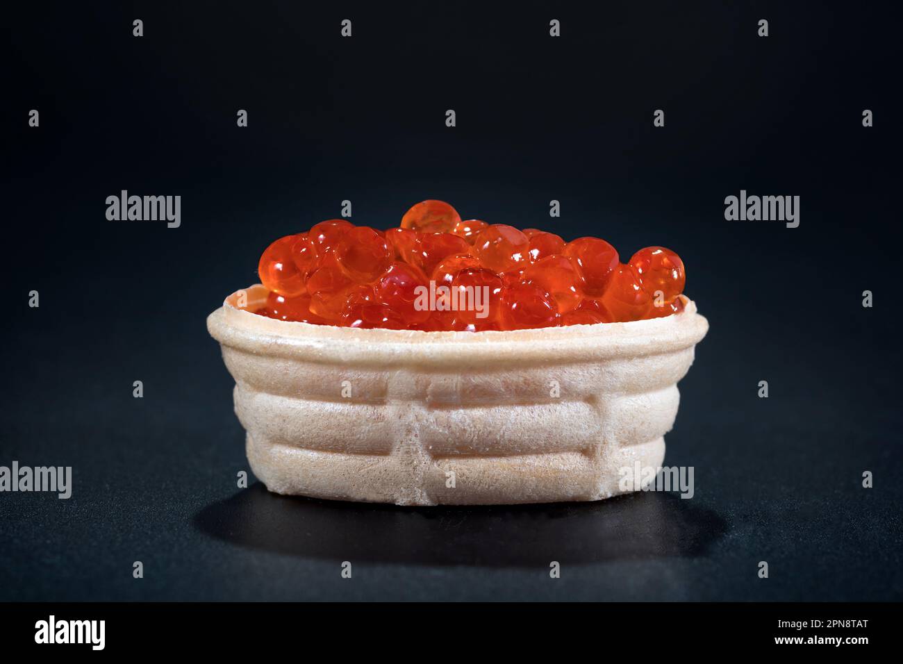Tartlet with red caviar on a black background. Structure of caviar of a ...