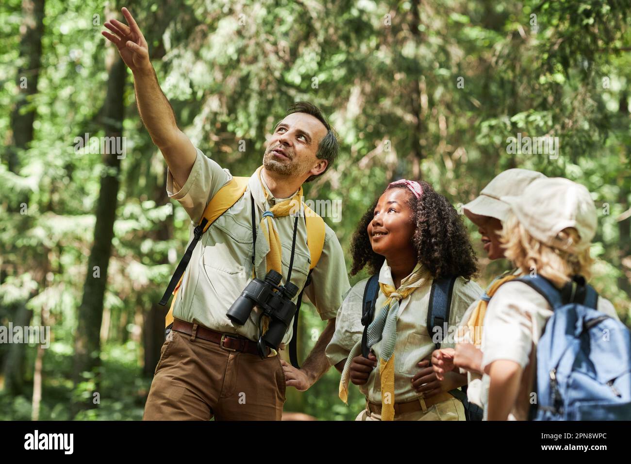 Diverse group of scouts hiking in forest with adult leader pointing ...
