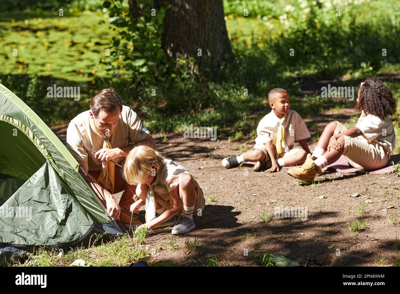 Group of scouts setting tent during hiking trip in forest scene lit by ...