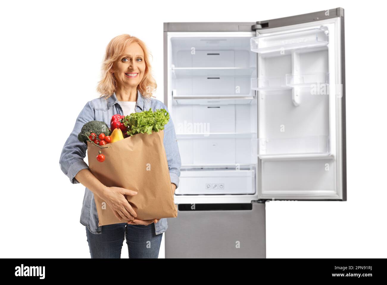 Woman with a grocery bag posing in front of an open empty fridge ...