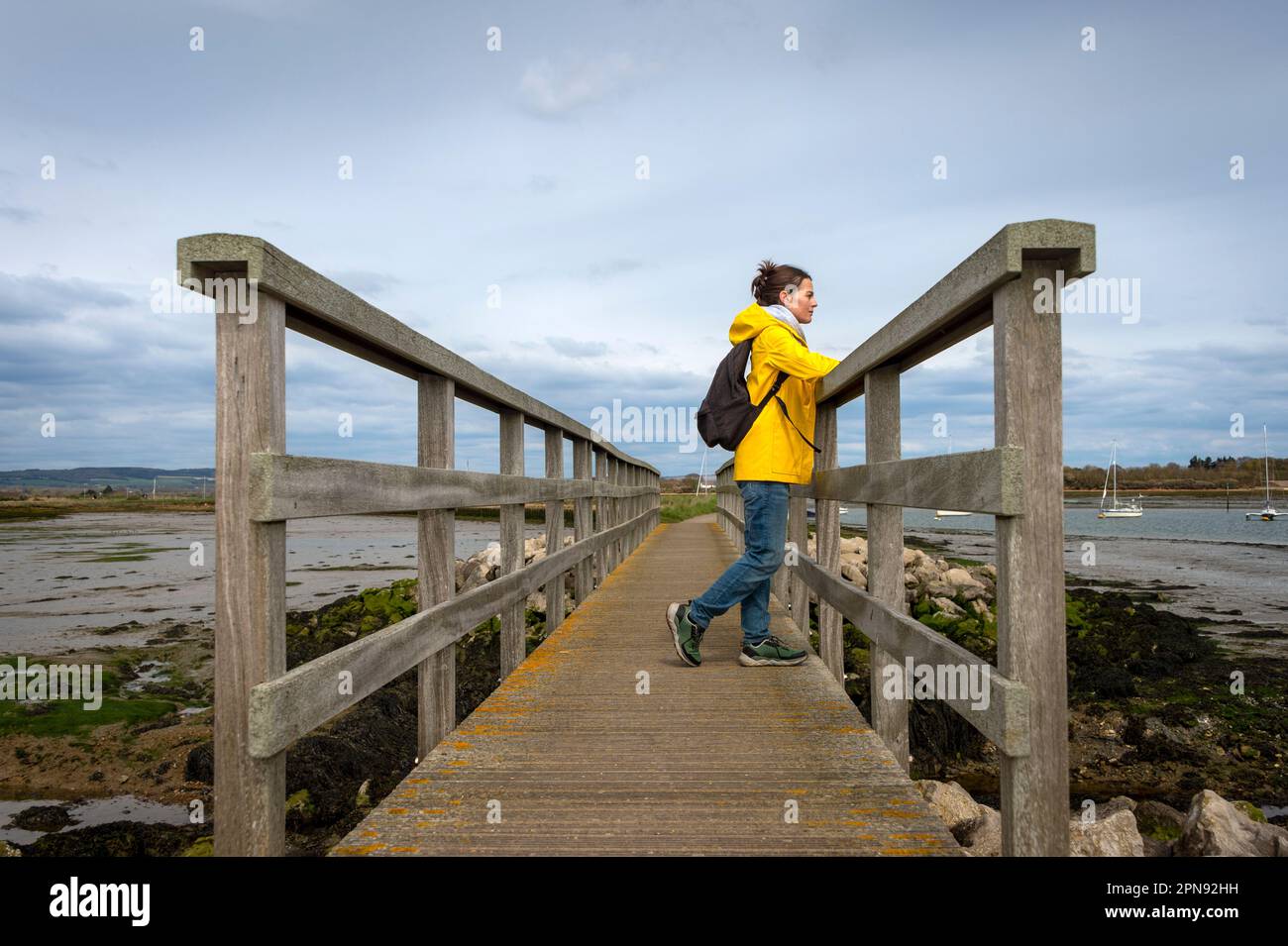 Mid adult woman wearing a yellow coat leaning on a bridge looking at ...