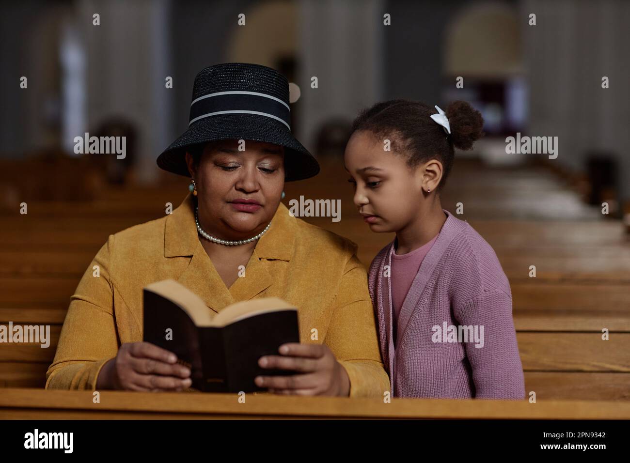 Grandmother reading Bible to her granddaughter while they sitting on bench in church Stock Photo ...