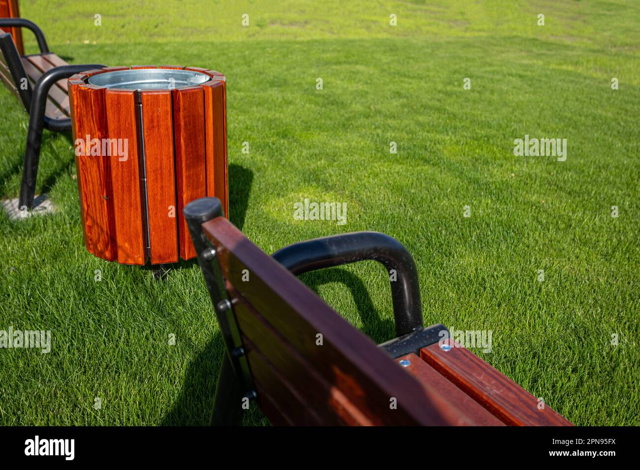The trash can stands right next to a bench near the green lawn Stock ...