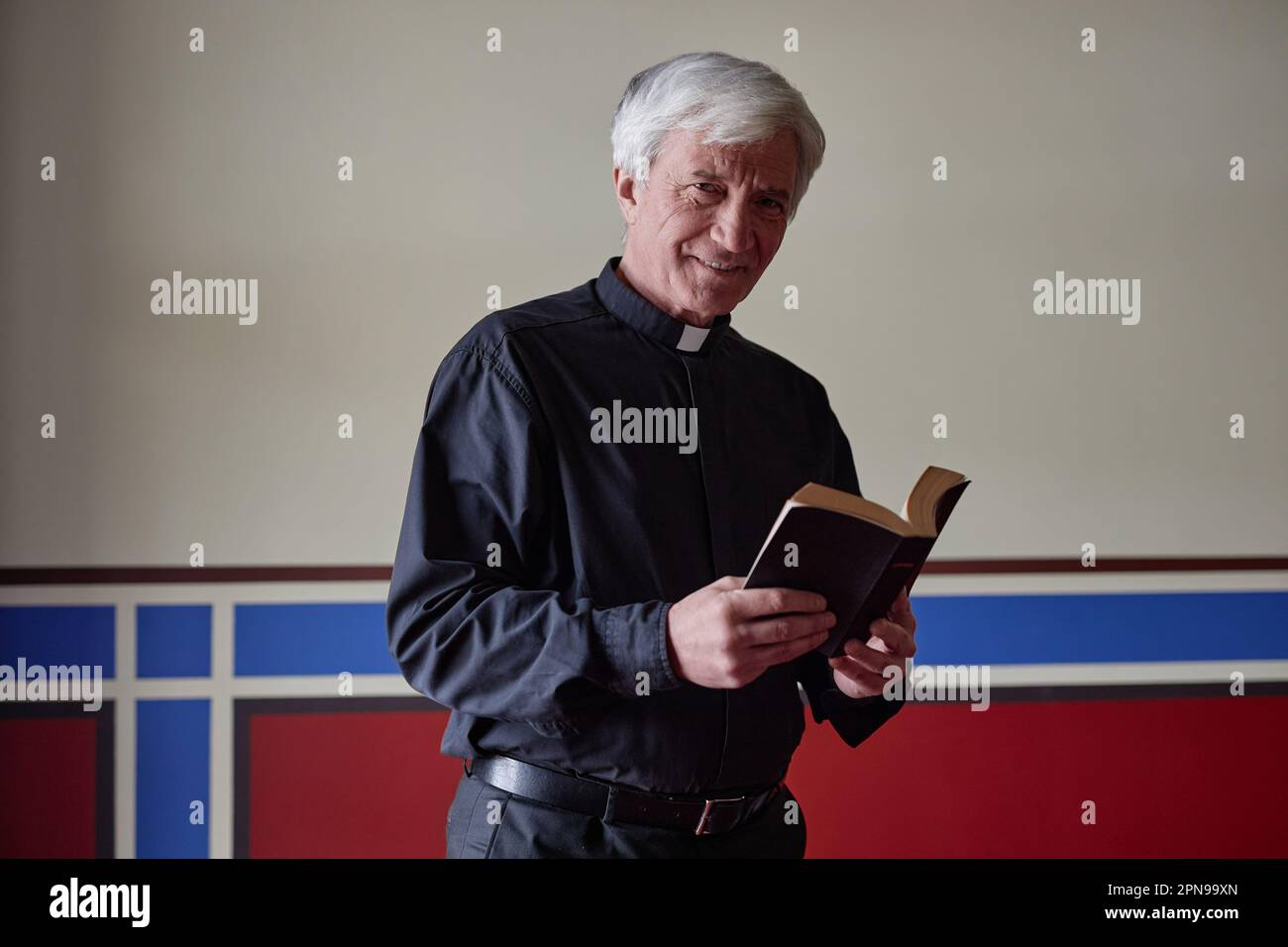 Portrait of senior priest smiling at camera while reading prayer in ...