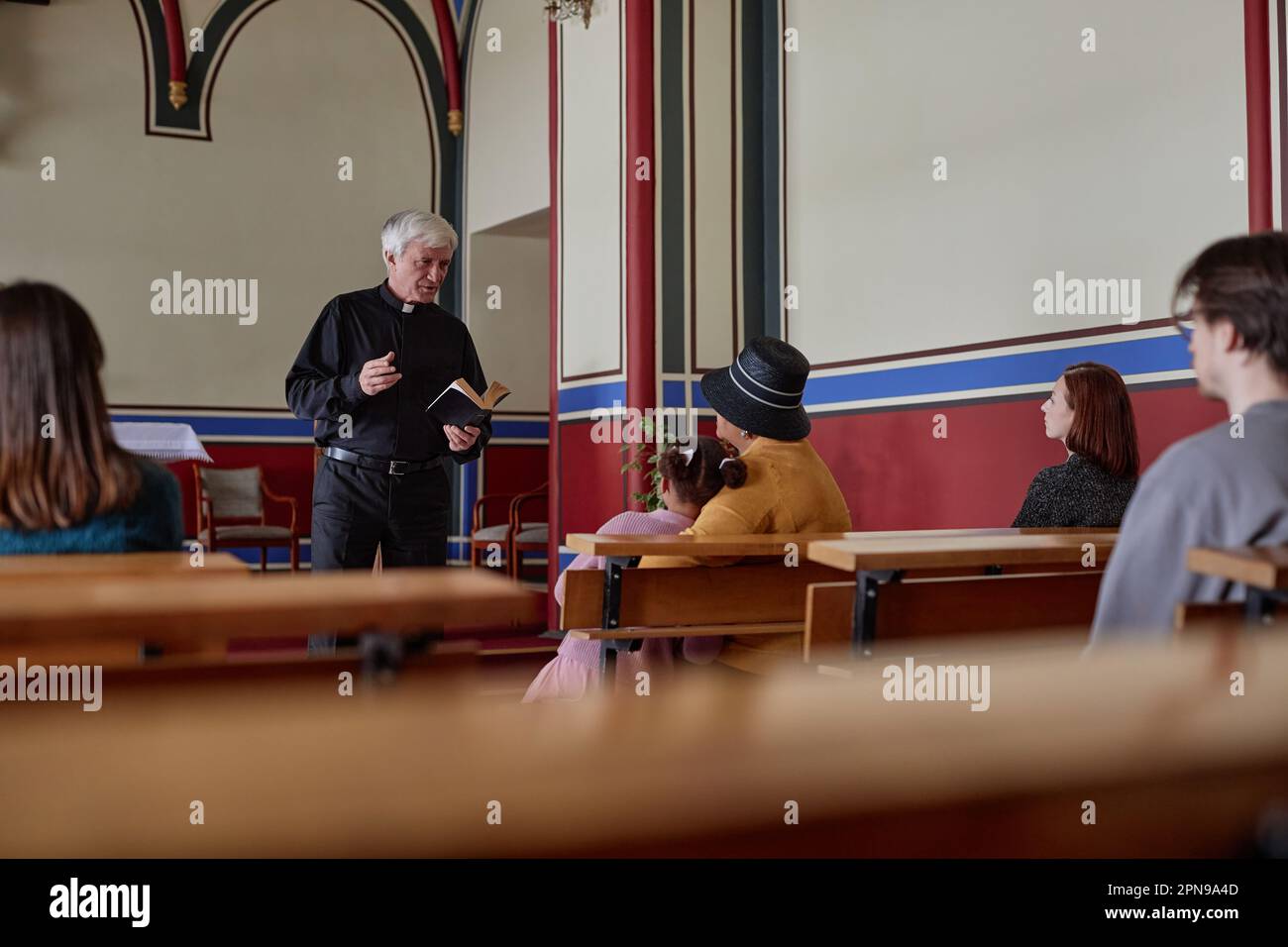 Senior priest holding book and reading sermon for believer people who ...