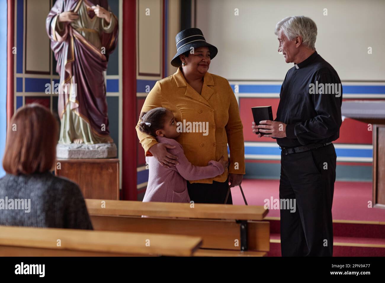 Grandmother with her granddaughter talking to priest while standing in ...