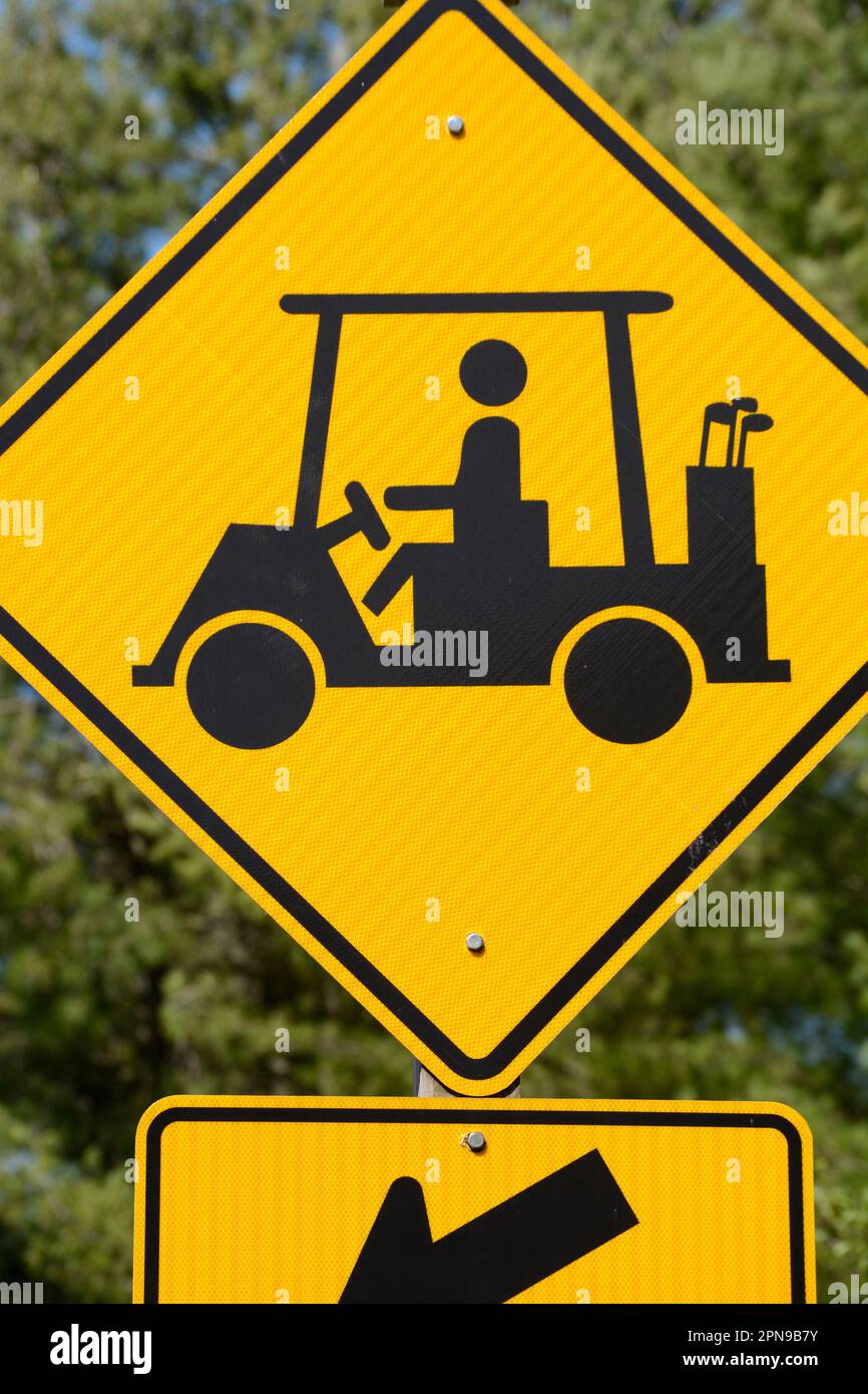 A golf cart crossing sign along a road warns motorists to watch for ...