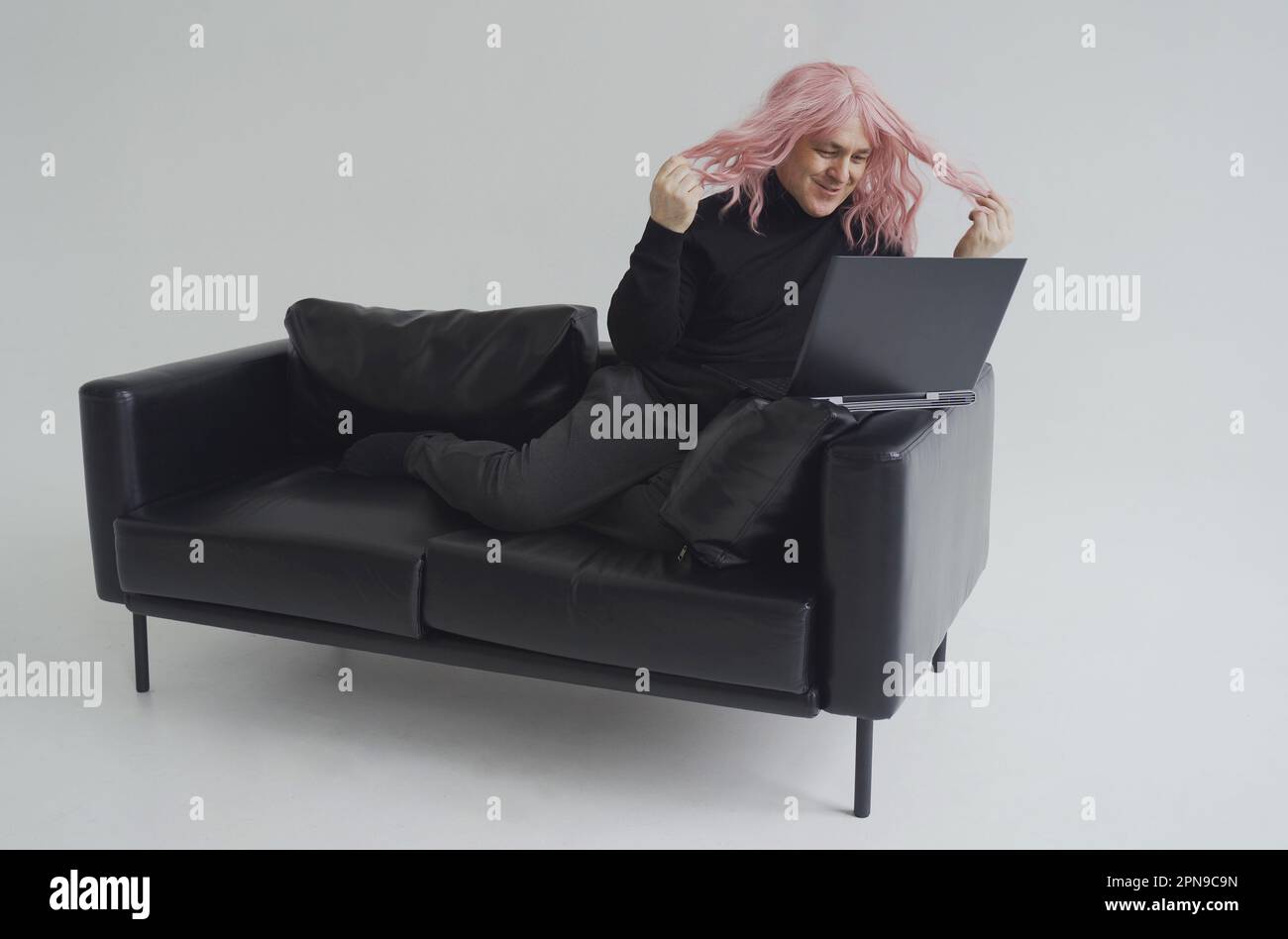 Portrait of a smiling man in a pink wig, sits on a sofa, communicates ...