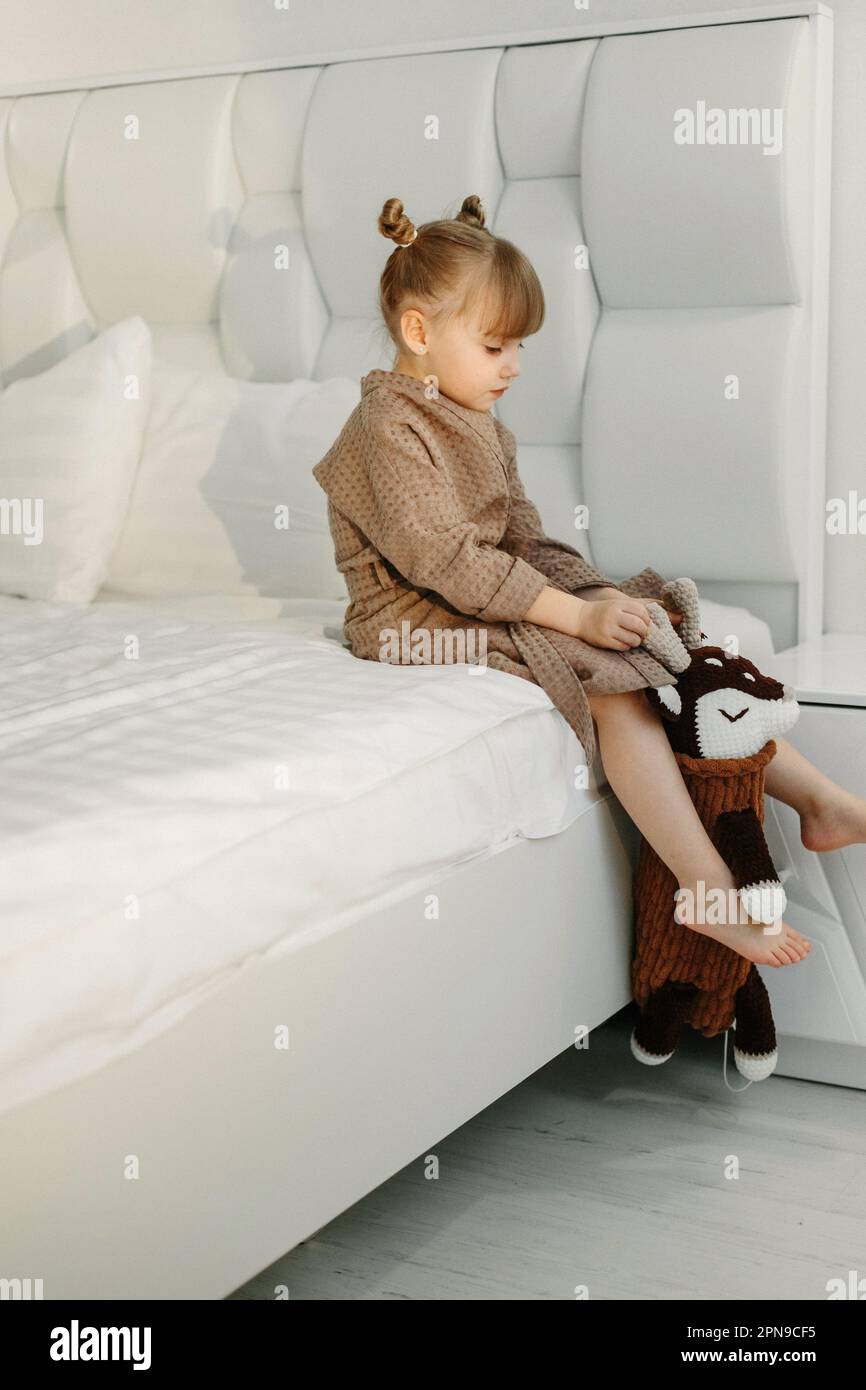 A girl in a dressing gown plays in bed with knitted toys Stock Photo ...