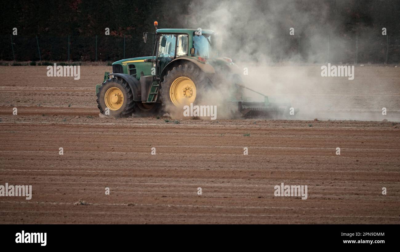 Tractor ploughing a field shrouded in the dust of dry soil from the ...