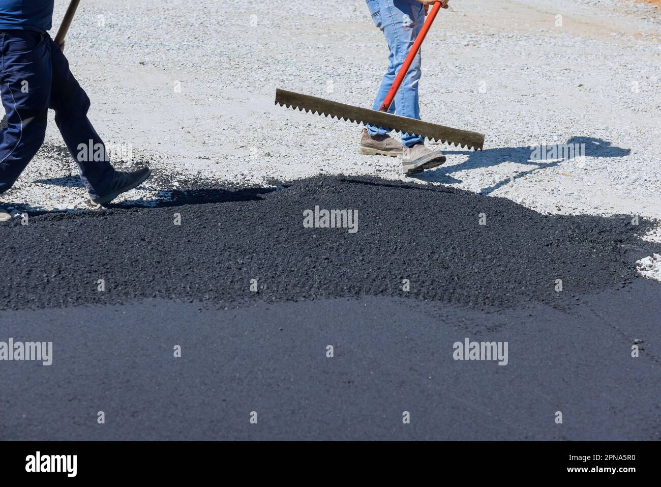 Workmen working on pavement of road are laying asphalt while shoveling ...
